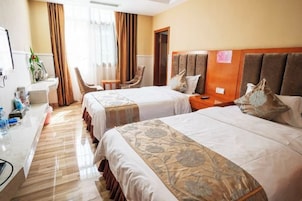 Quarto de hotel com duas camas, uma escrivaninha, uma cadeira e uma mesinha.