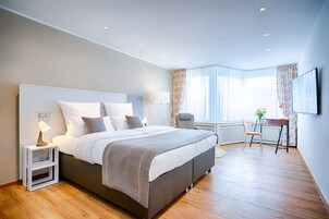 Quarto moderno com cama grande, mesas de cabeceira, escrivaninha e uma cadeira.