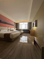 Quarto de hotel com duas camas, uma janela grande, um quadro na parede e uma televisão montada.