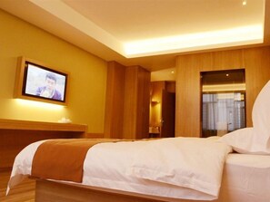 Quarto de hotel com uma cama, uma televisão fixada na parede e cabeceira de madeira.