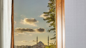 Janela com vista para um horizonte urbano, incluindo uma mesquita com um minarete, e uma cadeira em primeiro plano.