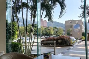 Vista da janela com palmeiras, uma estrada e um edifício com uma placa.