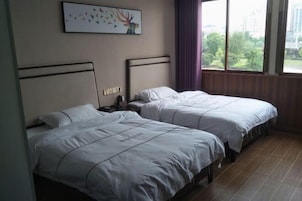 Quarto de hotel com duas camas, uma mesa de cabeceira, uma luminária na parede e uma janela com vista para o verde.