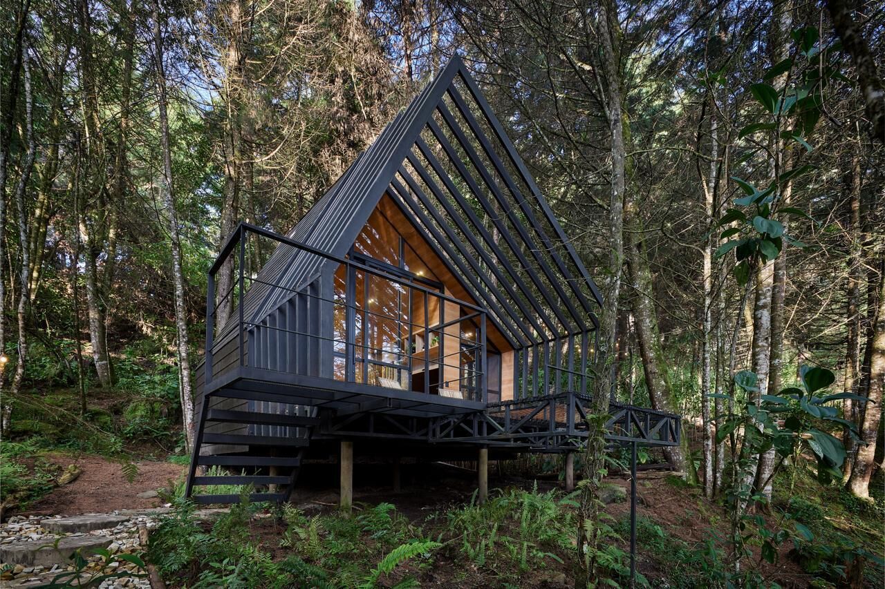 Uma cabana moderna com telhado inclinado, grandes janelas e um deck de madeira.