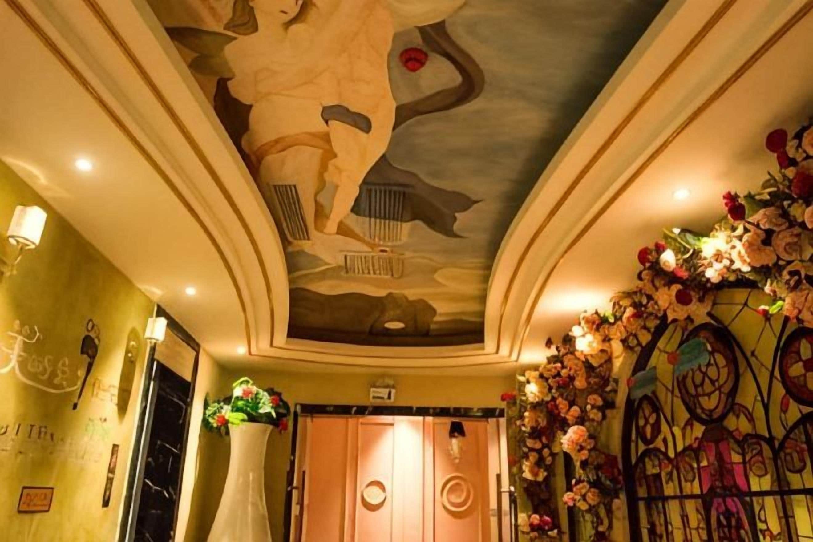 Um saguão de hotel com teto decorativo, balcão de recepção e arranjos florais.