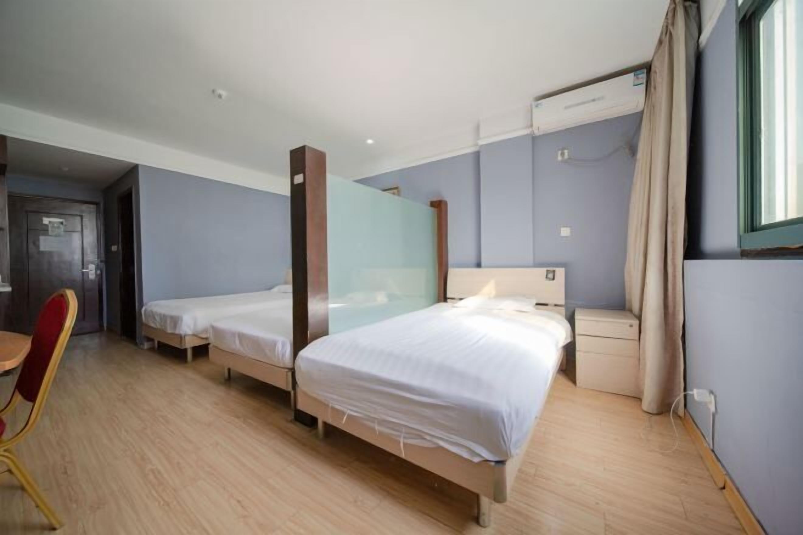 Quarto de hotel com duas camas de solteiro, uma pequena escrivaninha, uma cadeira e uma janela com cortinas.