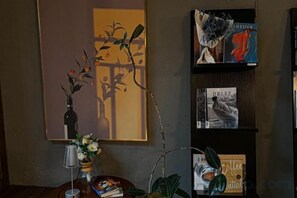 Quarto com estante, uma obra de arte emoldurada e uma mesinha com abajur e livros.