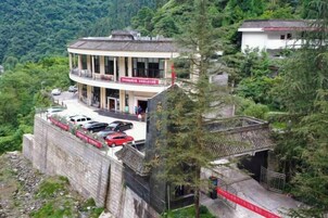Edifício de vários andares com varanda, cercado por vegetação e um muro de pedra.
