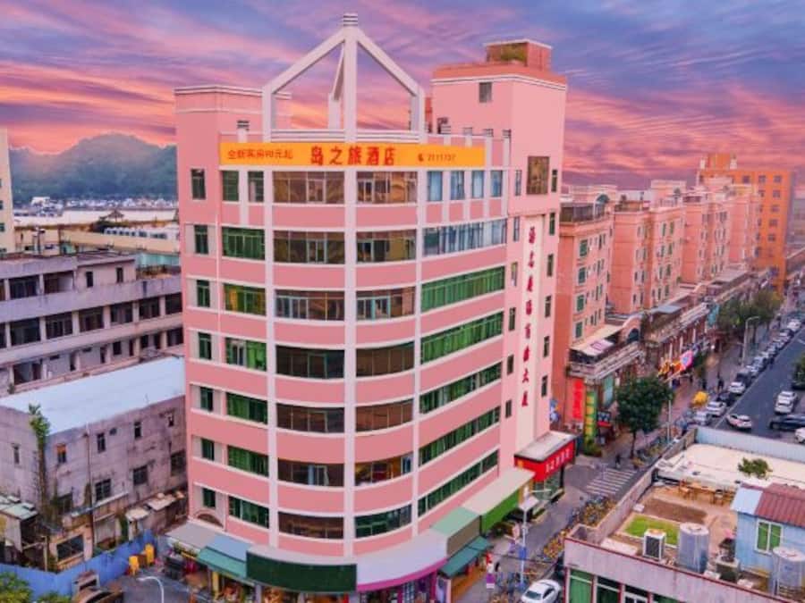 Um edifício de vários andares com uma placa grande no topo, rodeado por outros edifícios e uma rua.