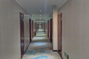 Um corredor longo e estreito de hotel, com carpete estampado e portas de ambos os lados.