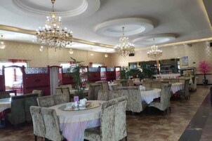Um restaurante com mesas redondas, cadeiras, lustres e uma parede com padrão.