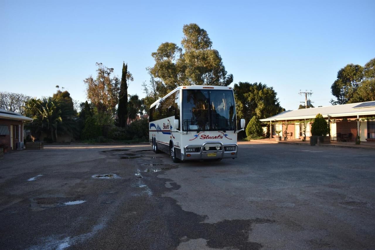 Um ônibus estacionado em um estacionamento, com árvores e edifícios ao fundo.