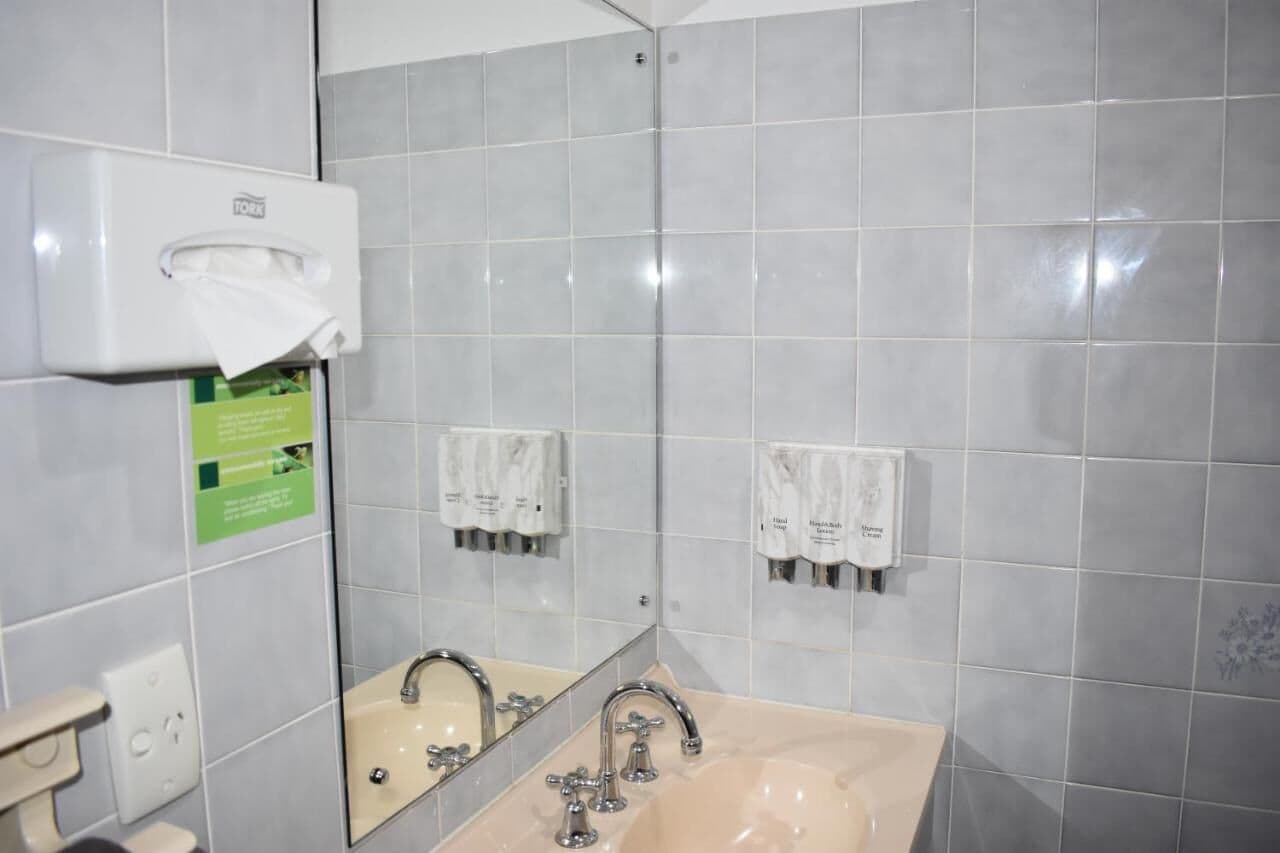 Casa de banho com lavatório, espelho e dois dispensadores de papel.