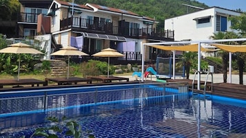 Piscina com deck revestido, rodeada por espreguiçadeiras e guarda-sóis.