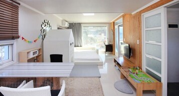 Quarto de hotel moderno com cama, televisão, um espaço de brincadeira pequeno e janela com persianas.