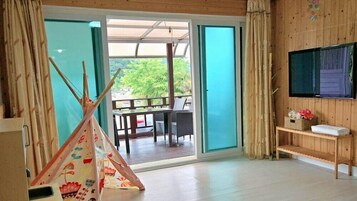 Quarto com porta de vidro deslizante para um deck externo, um suporte de TV de madeira e uma tenda tipi colorida.