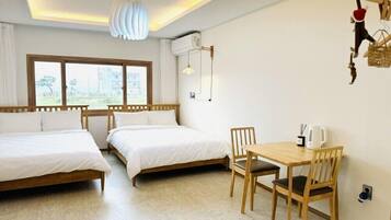 Quarto de hotel com duas camas de solteiro, uma mesa de madeira com cadeiras, luminária pendente e vista para o exterior através de amplas janelas.