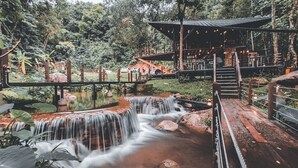 Uma cascata com uma ponte de madeira e uma estrutura de madeira com telhado em uma área arborizada.