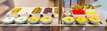 Buffet com diversos alimentos, incluindo patês, picles, azeitonas e legumes.