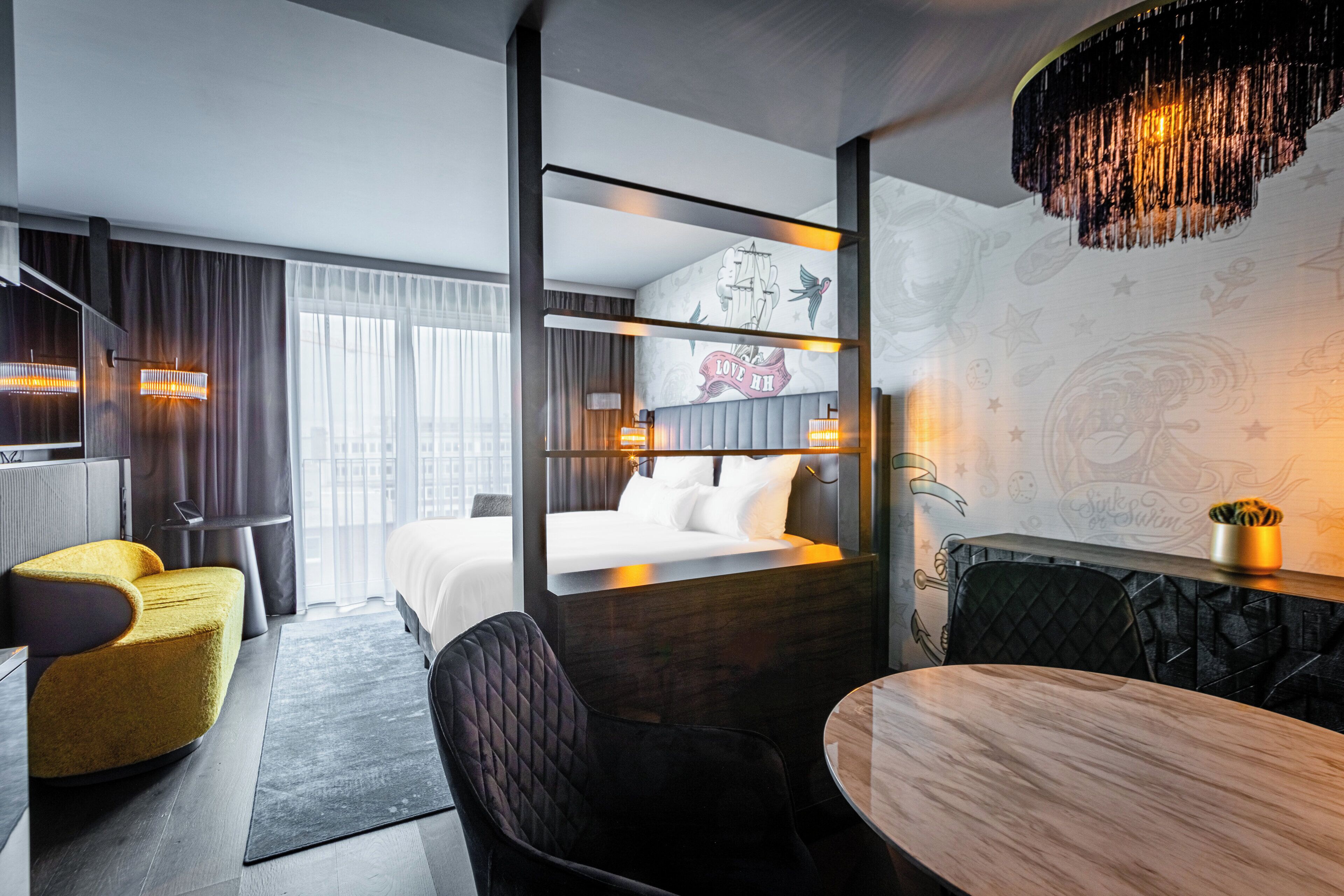 Quarto de hotel moderno com cama, escrivaninha, cadeira, mesa pequena e decoração na parede.