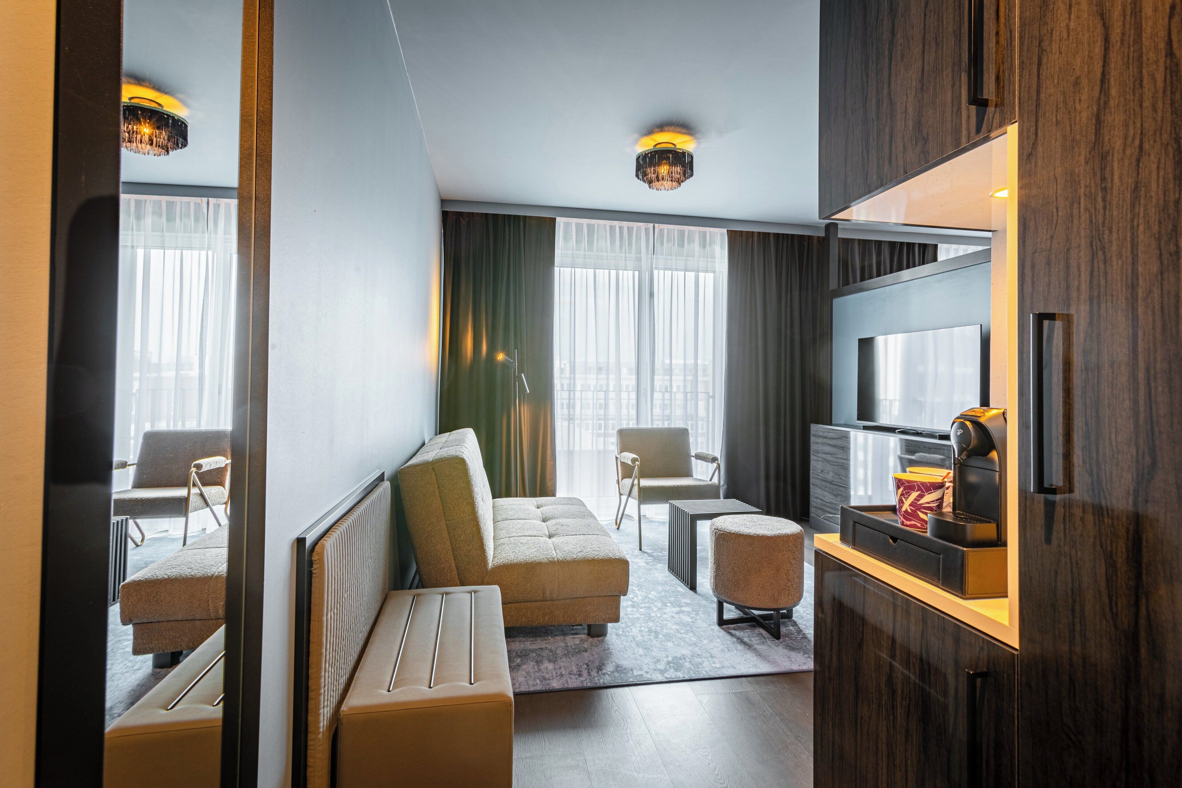 Quarto de hotel com sofá, poltrona e televisão sobre um armário de madeira.