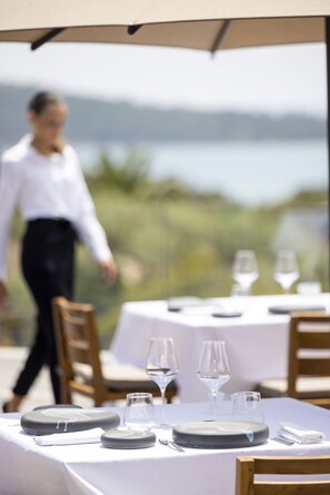 Mesa de jantar posta com pratos, copos e talheres, com vista para o exterior.