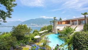 Área de piscina com espreguiçadeiras e guarda-sóis, cercada por vegetação exuberante e vista para o mar e montanhas.