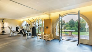 Uma academia com equipamentos de ginástica, um banco de madeira e uma grande janela com vista para um jardim.