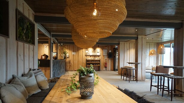 Um quarto espaçoso com uma longa mesa de madeira, um candeeiro tecido e um arranjo de plantas.