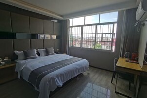 Quarto de hotel moderno com uma cama grande, uma escrivaninha e uma janela vista para a cidade.
