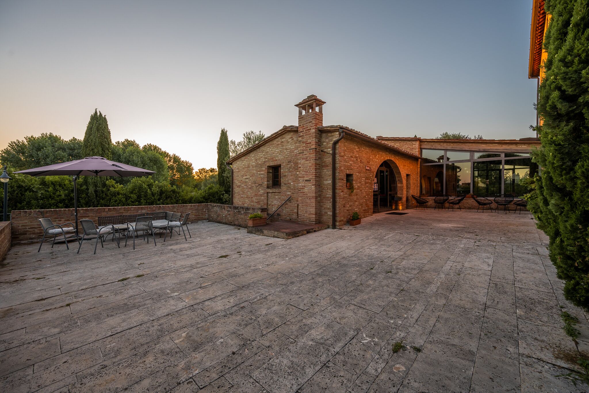 Edifício de tijolos com área de pátio, mobiliário externo e pérgola.