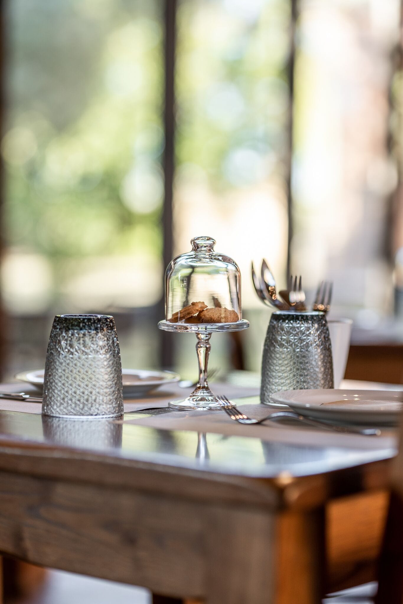 Uma mesa de jantar com um centro de mesa em cúpula de vidro, dois vasos texturizados e talheres.