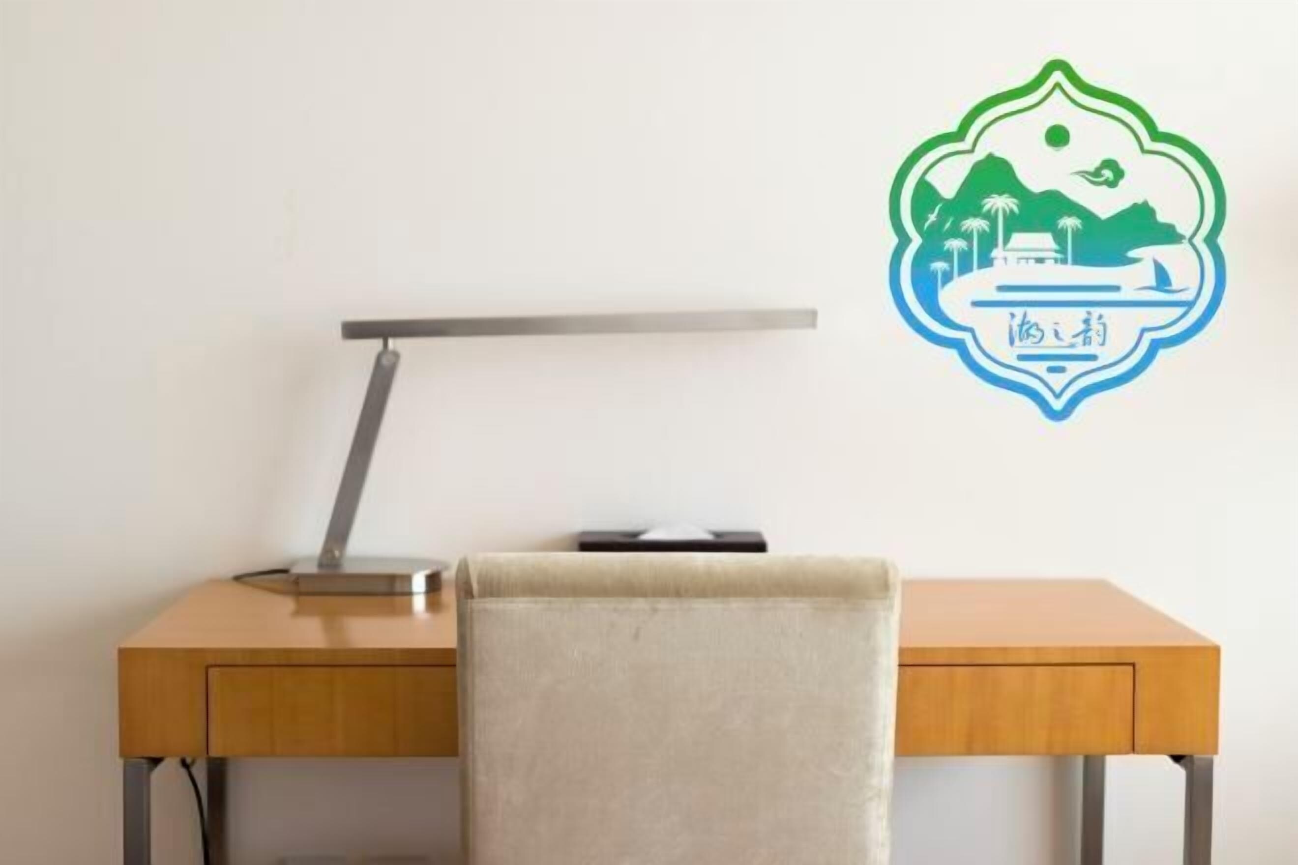 Uma mesa com uma luminária e uma cadeira, uma parede com um emblema verde e azul, e uma parede branca.
