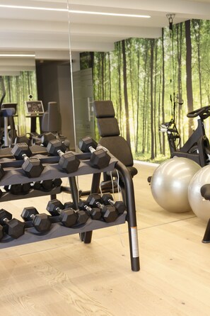 Uma academia com equipamentos de exercícios, incluindo halteres e bolas de ginástica, e um mural na parede com tema de floresta.