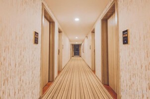 Corredor de hotel com piso revestido de carpete, portas em ambos os lados e placa indicando números de quartos.