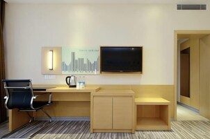 Quarto de hotel com escrivaninha, cadeira, televisão e cama.