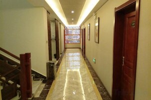 Um corredor com piso de mármore, portas de madeira e uma escada à esquerda.
