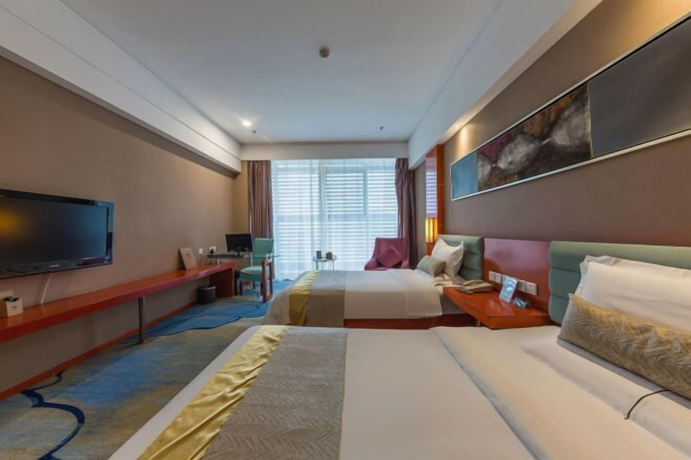 Quarto de hotel com uma cama grande, televisão, escrivaninha e janela com cortinas.