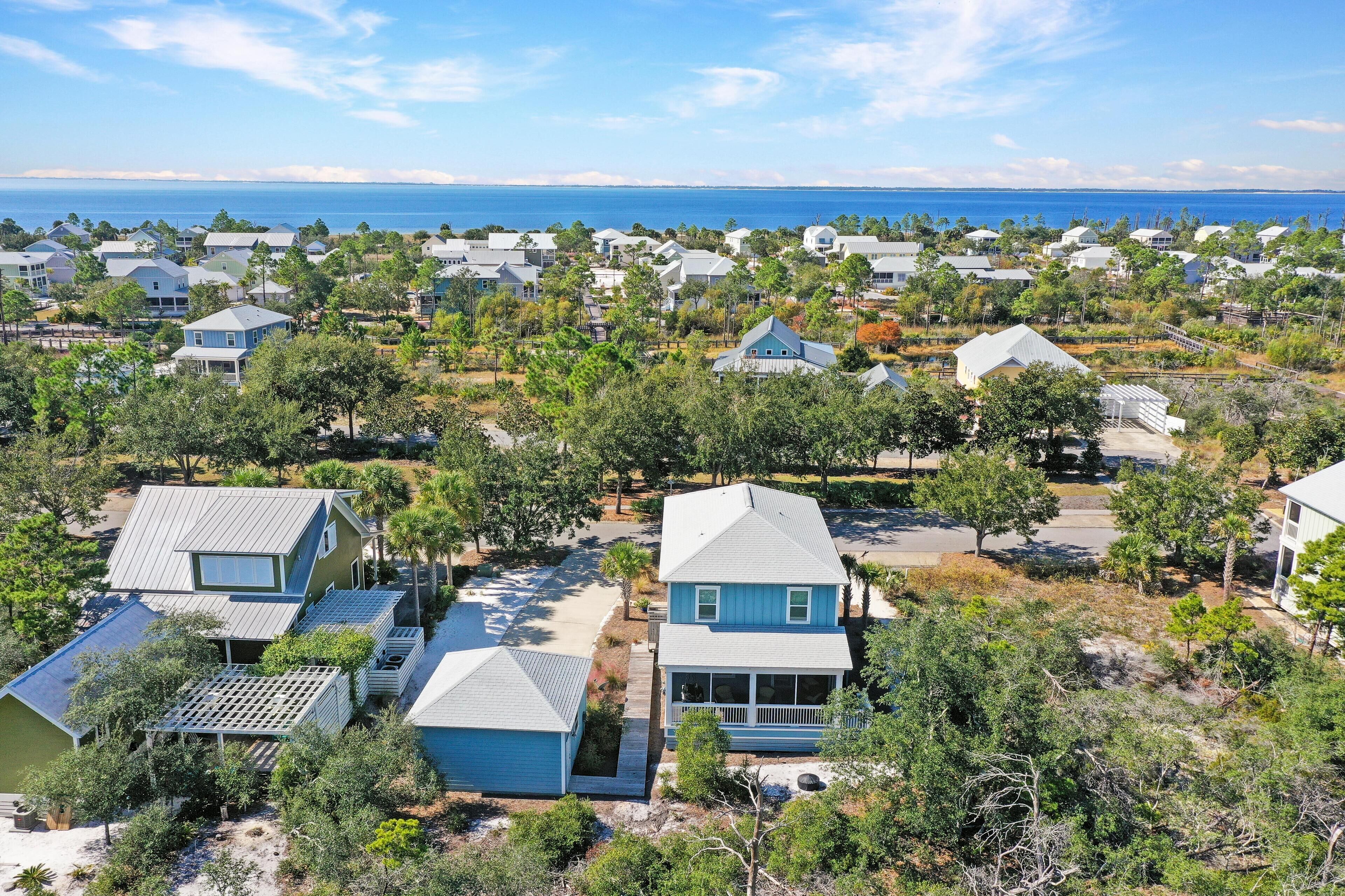 Uma área residencial costeira com casas de telhados pontudos e grandes janelas, rodeada por árvores e uma vista ampla do oceano.