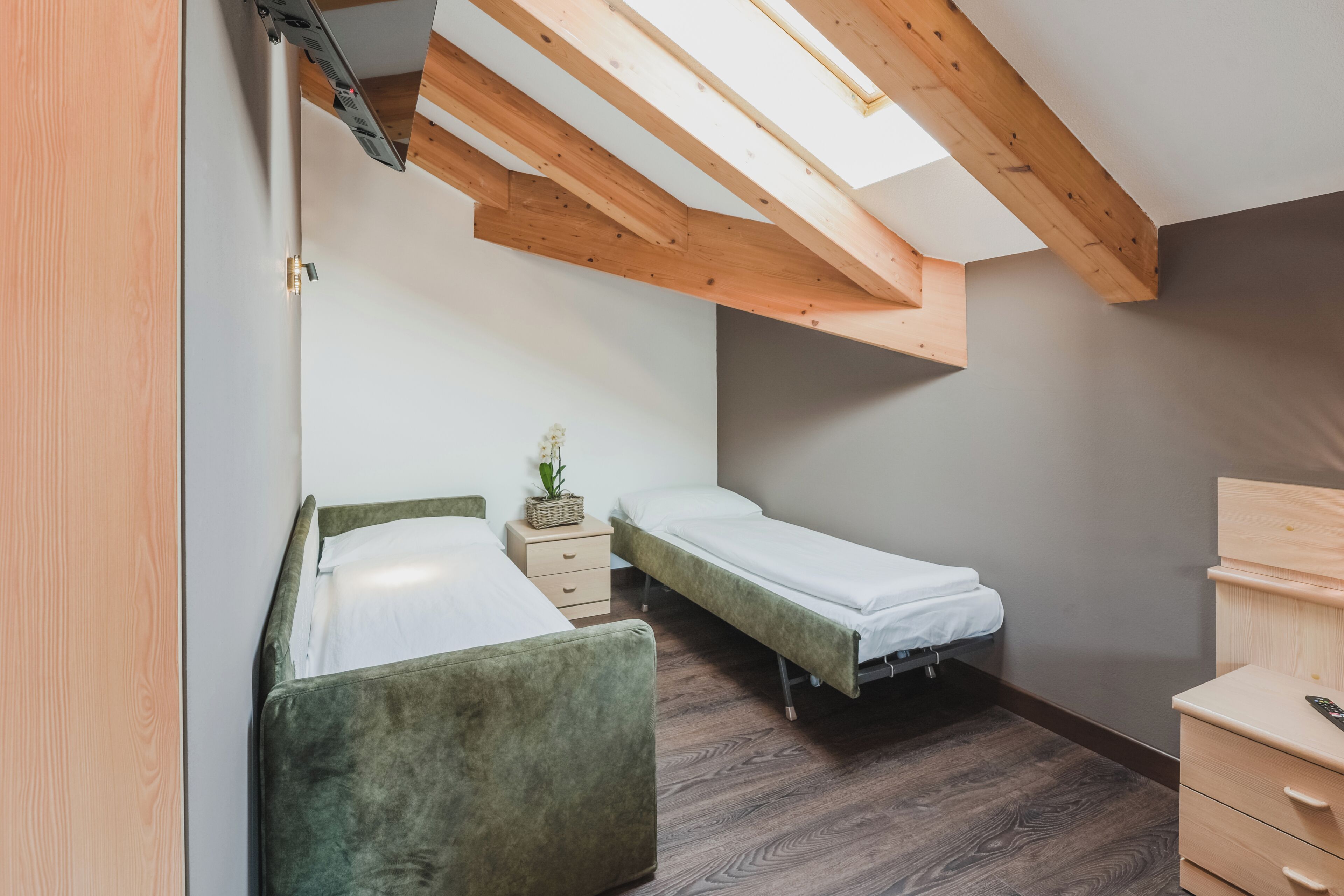 Quarto pequeno e compacto com duas camas de solteiro, uma cômoda de madeira e um claraboia.