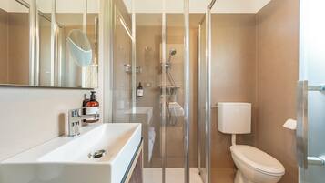 Uma casa de banho moderna com chuveiro envolto em vidro, lavatório branco e sanita.