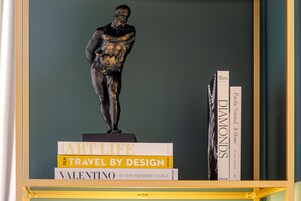 Uma estátua no topo de uma pilha de livros, incluindo títulos como 'Art Life' e 'Travel by Design'.