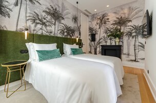 Quarto com duas camas, cabeceira verde, uma mesinha, lareira e uma parede com um mural de palmeira.