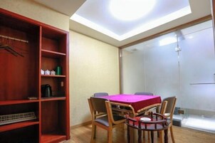 Quarto com claraboia, mesa com toalha vermelha, cadeiras de madeira e estante com diversos objetos.