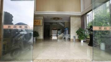Entrada de hotel com balcão de recepção, escada e plantas em vasos.