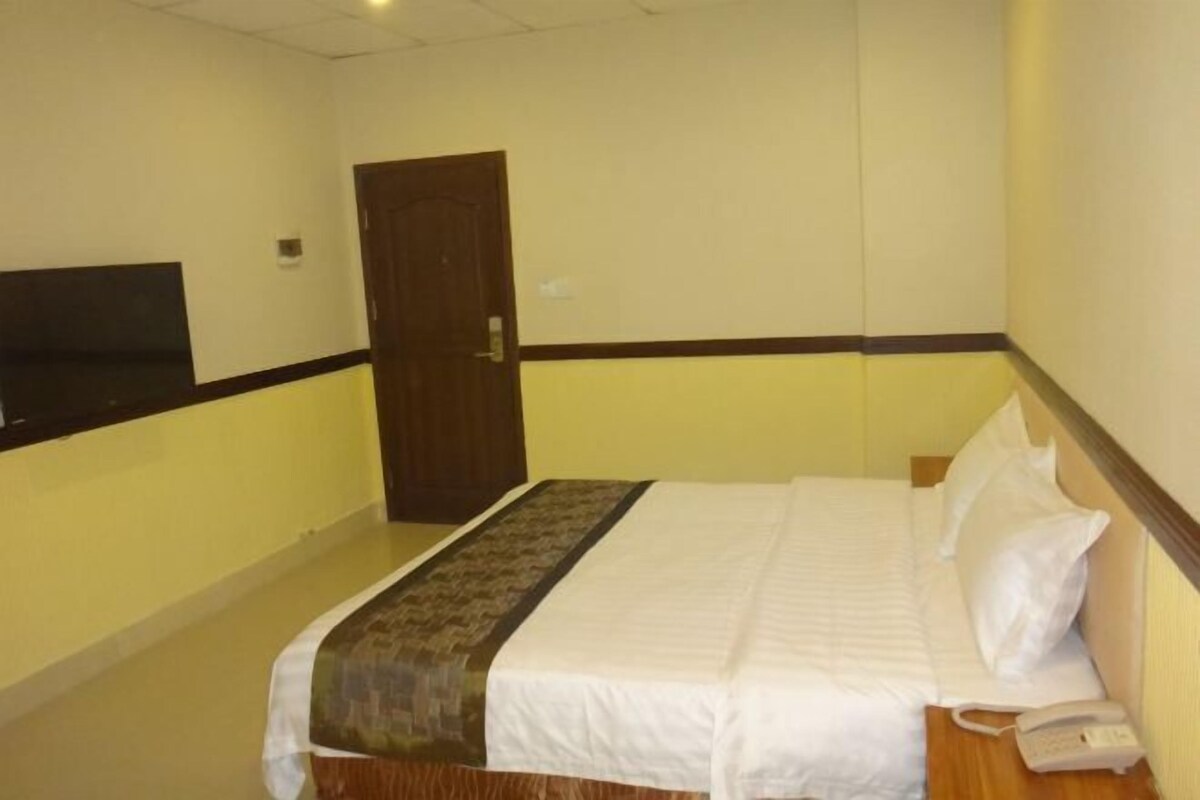 Quarto de hotel com uma cama, telefone ao lado e uma porta.