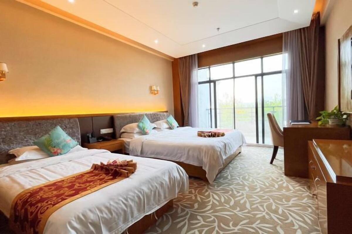 Quarto de hotel com duas camas, uma escrivaninha e uma janela grande.