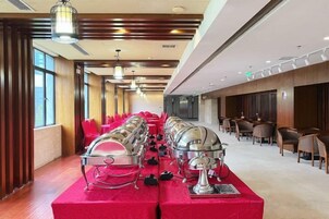 Salão de banquetes com longas mesas, cadeiras e estações de buffet.