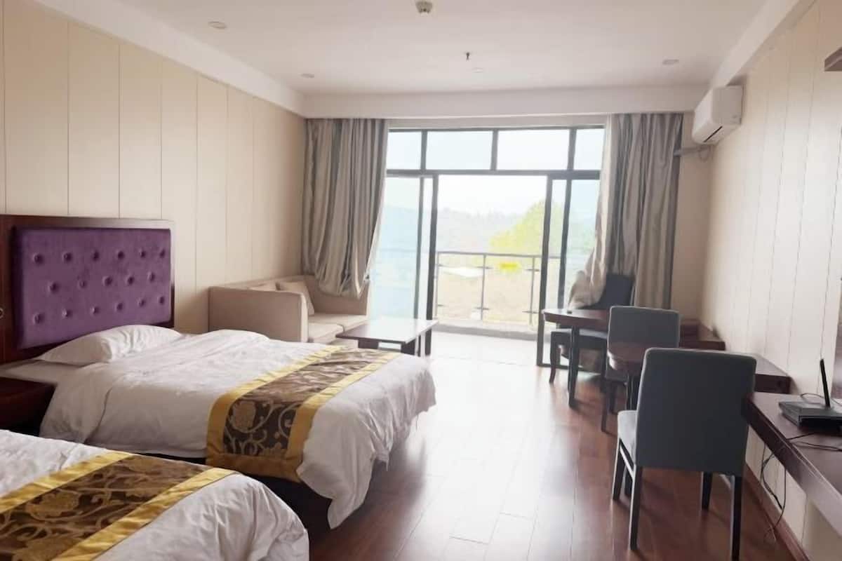 Quarto de hotel com duas camas, uma escrivaninha, uma cadeira e vista para o exterior.