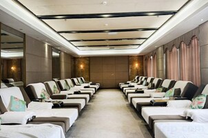 Quarto de hotel com fileira de cadeiras de massagem, um espelho grande e design moderno no teto.